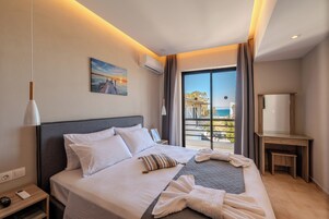 Quarto de hotel com uma cama, mesa de cabeceira, escrivaninha, janela grande com vista e ar condicionado.