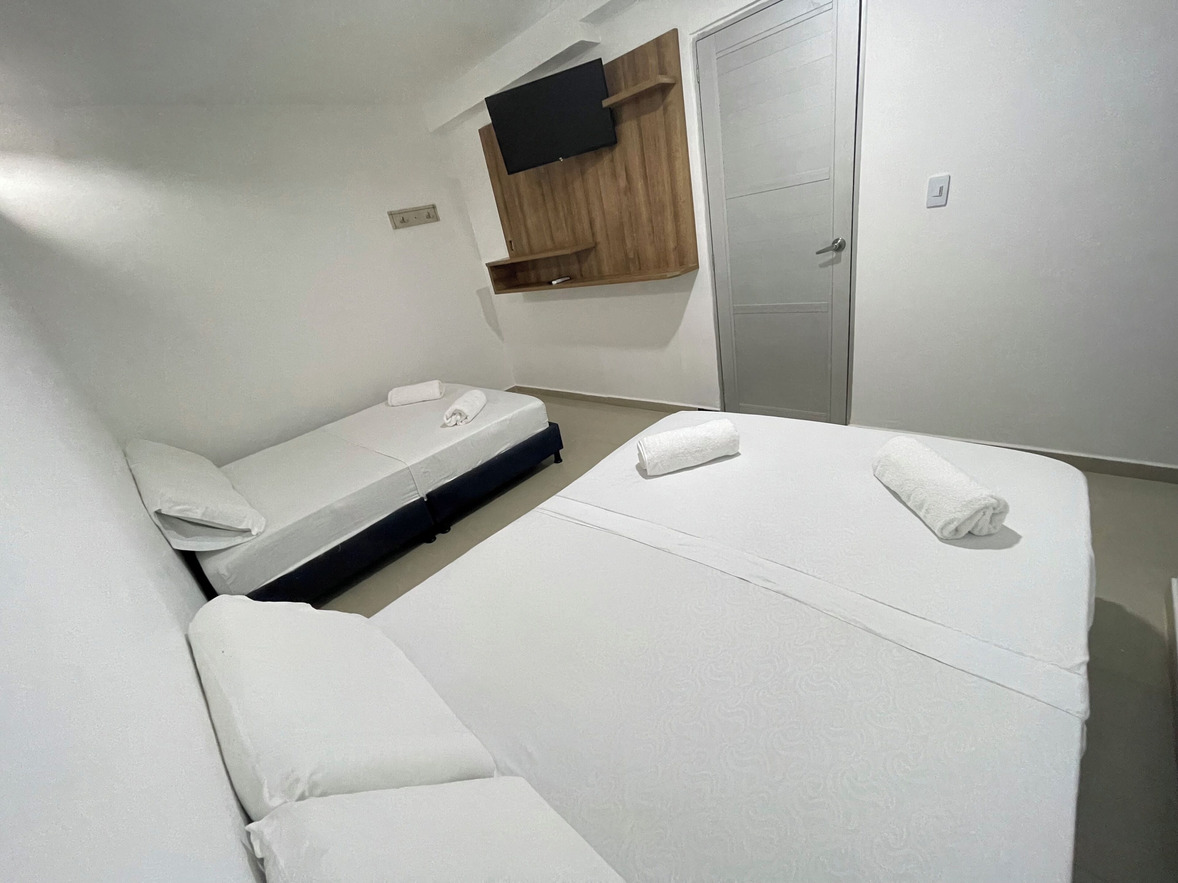Quarto com duas camas, um guarda-roupa, televisão montada na parede e uma tomada.