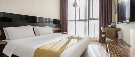 Quarto de hotel com uma cama grande, uma escrivaninha e uma televisão.