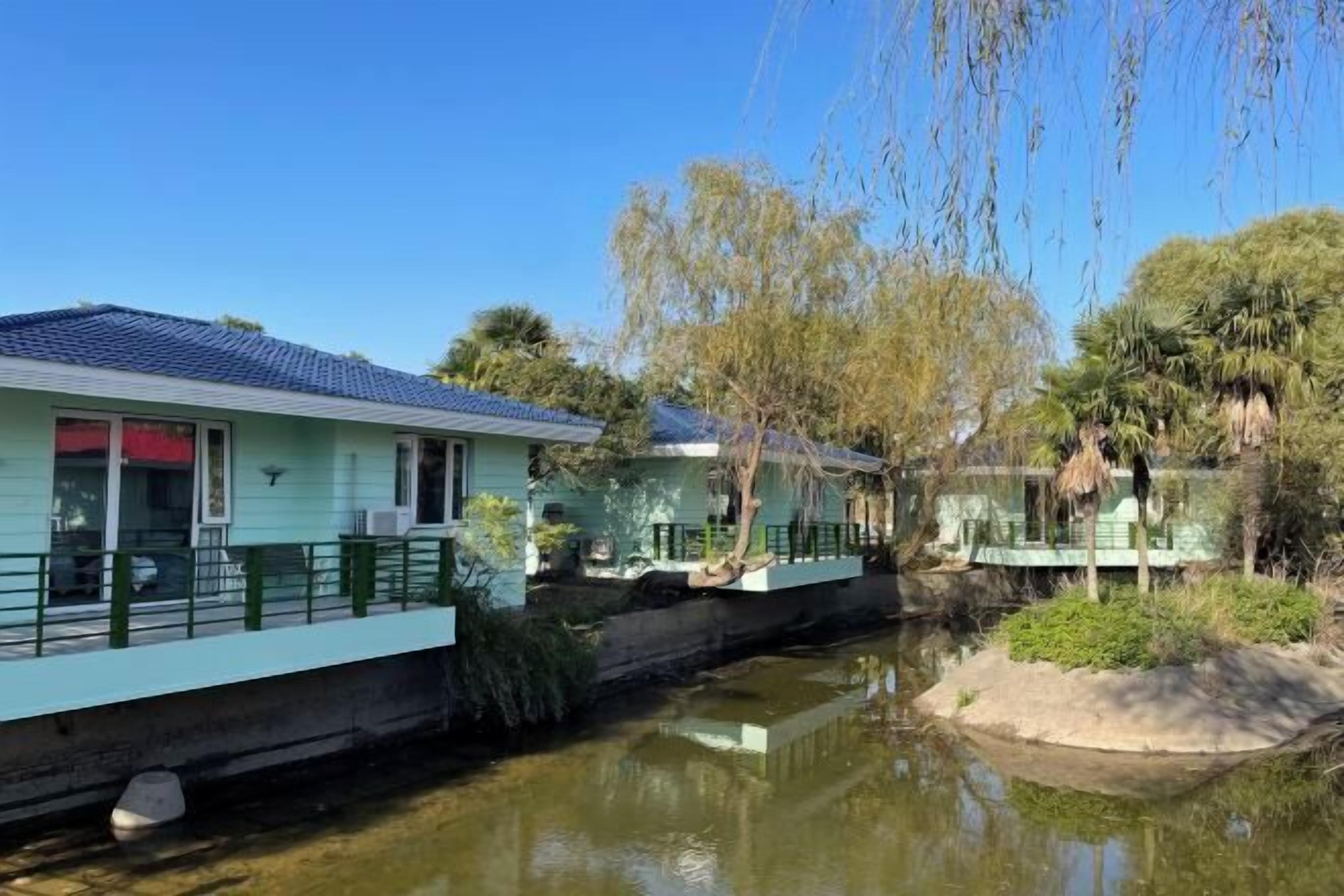 Fileira de cabanas verde-claras com um pequeno lago em primeiro plano.