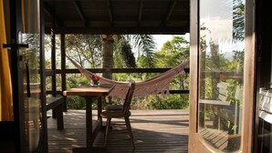 Uma porta aberta dá acesso a um deck de madeira com uma rede, uma mesa e uma cadeira.