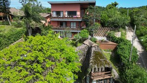 Um edifício com vários andares e varandas, cercado por vegetação exuberante e uma construção com telhado de palha.