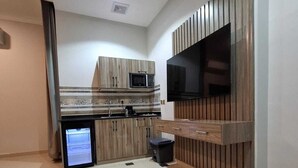 Uma cozinha moderna com micro-ondas embutido, geladeira e TV de tela plana instalada em uma parede de painéis de madeira.