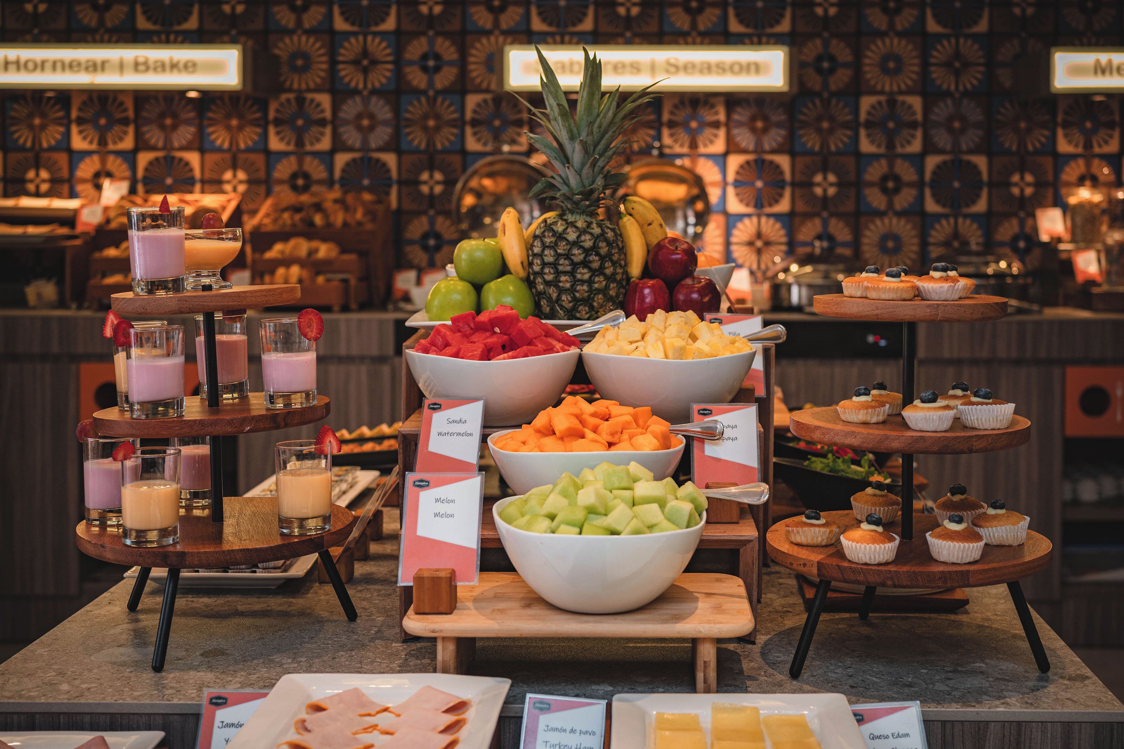 Buffet com diversos alimentos e bebidas, incluindo frutas, legumes e sobremesas.
