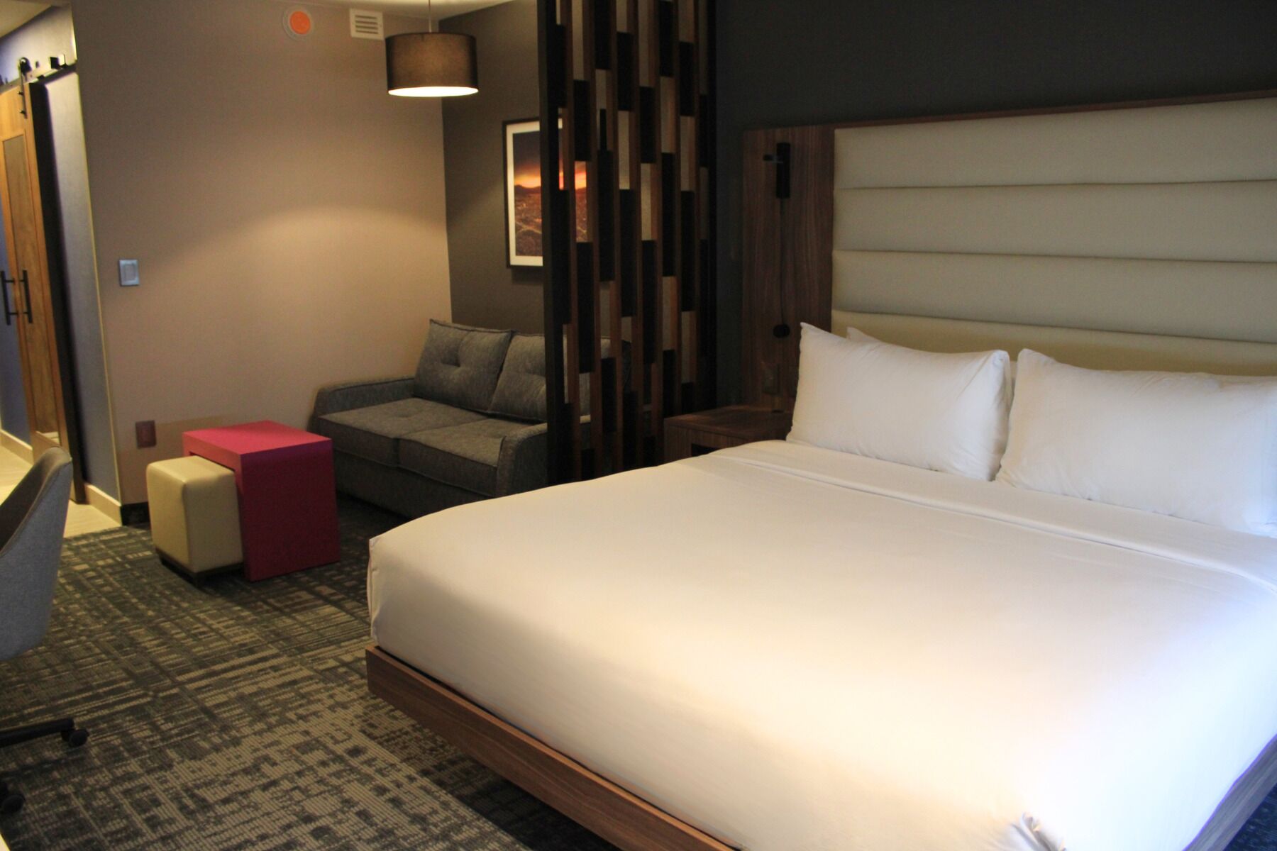 Quarto de hotel com uma cama grande, um sofá, uma mesinha e uma cadeira.