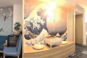 Quarto com pintura tradicional japonesa de ondas, uma mesa de recepção, uma cadeira azul e uma planta.