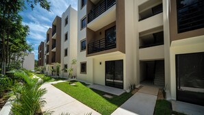 Um edifício residencial moderno de vários andares, com varandas, um gramado bem cuidado e céu claro.