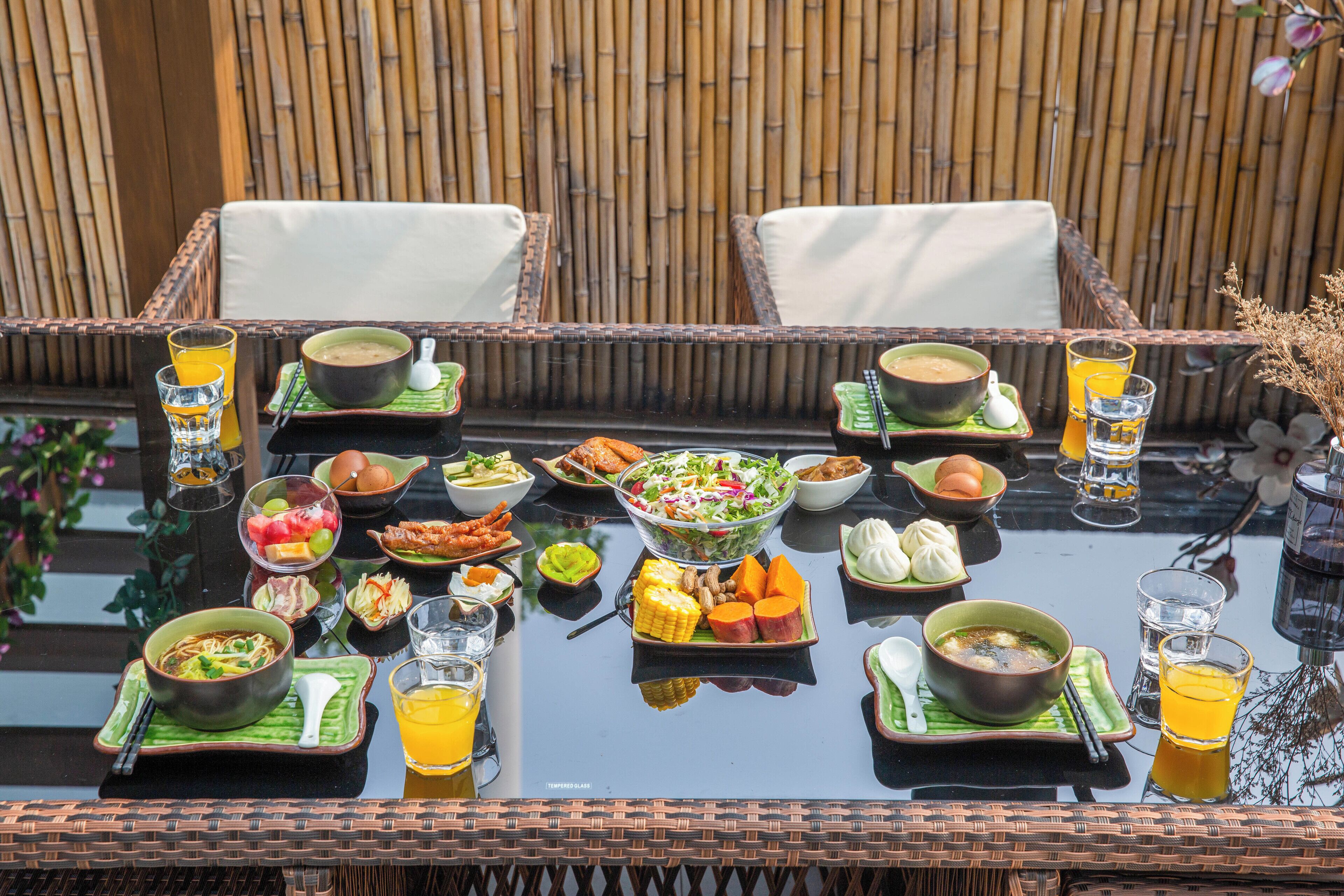 Mesa de jantar posta com diversos pratos e bebidas, rodeada por cadeiras de vime.