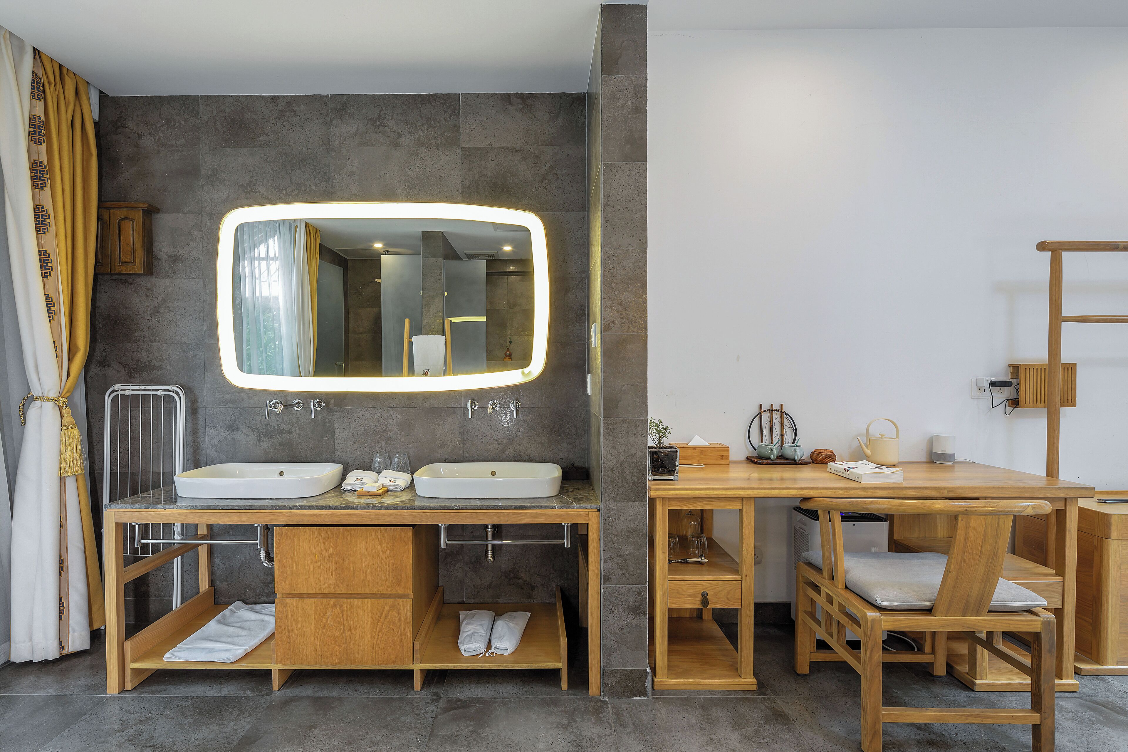 Uma casa de banho moderna com duas lavatórios, um espelho grande e um toucador de madeira com uma cadeira.