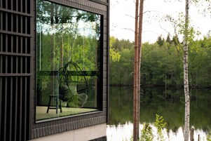 Uma cabana com uma grande janela com vista para um lago tranquilo e uma floresta densa.