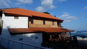 Um edifício de dois andares com telhado de telhas vermelhas, varanda e vista para o oceano.