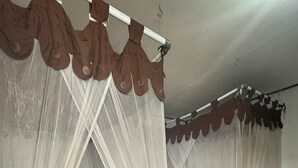 Duas camas de madeira com roupa de cama branca e cabeceiras castanhas, cada uma com mosquiteiro.