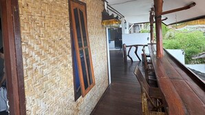 Área externa coberta com um banco de madeira e uma mesa, parede de tecido e ventilador de teto.