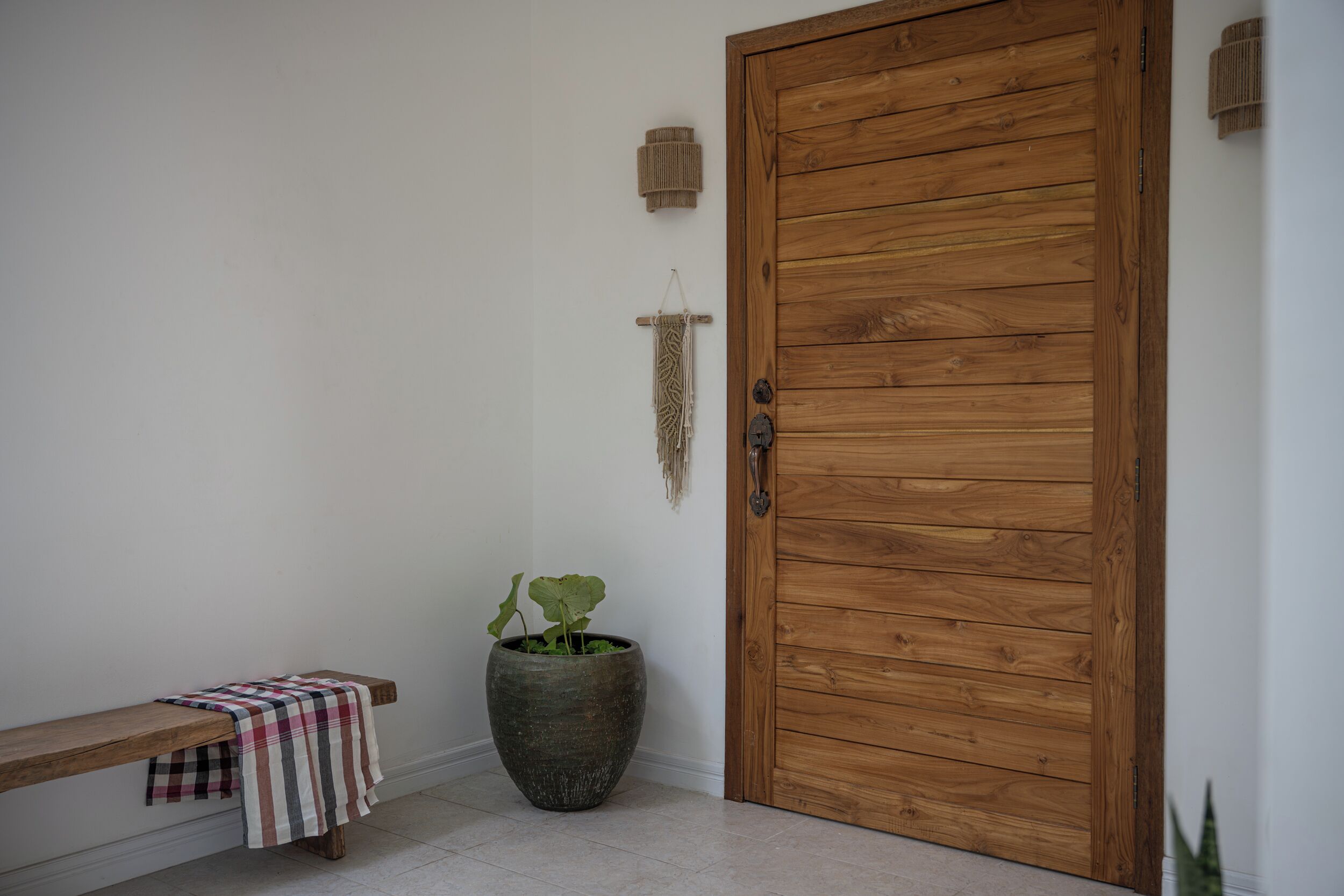 Uma porta de madeira, um banco com um cobertor xadrez e uma grande planta em vaso.