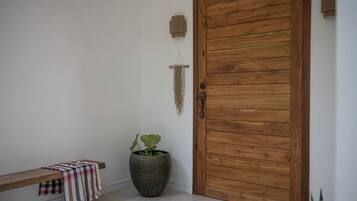 Uma porta de madeira, um banco com um cobertor xadrez e uma grande planta em vaso.