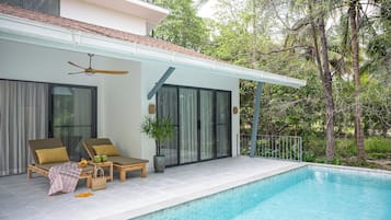 Uma área moderna junto à piscina, com espreguiçadeiras, um ventilador de teto e um vaso de planta.