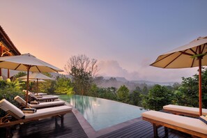 Uma piscina infinita com espreguiçadeiras e guarda-sóis, cercada por vegetação exuberante e um cenário montanhoso.