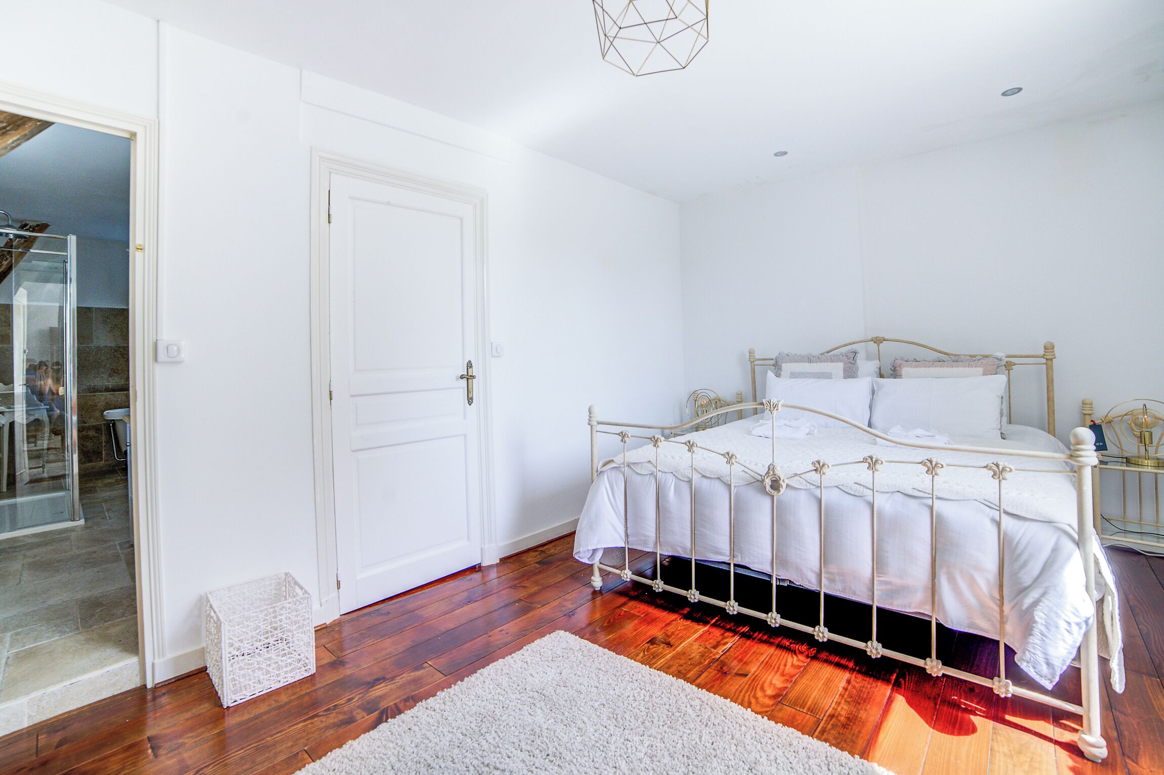 Quarto com cama branca, soalho de madeira e porta branca.