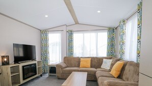 Uma sala de estar com sofá, mesa de centro, TV sobre um suporte de madeira e lareira.