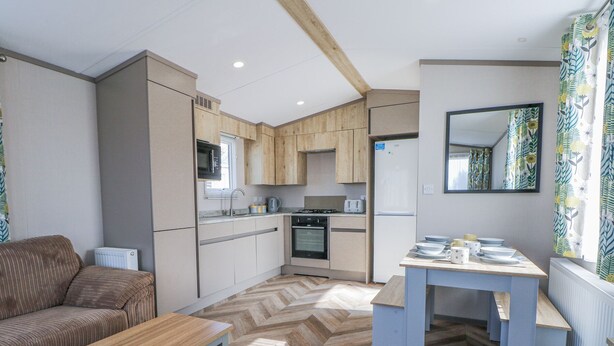 Um espaço compacto com cozinha compacta, sofá, mesa pequena e piso com padrão herringbone.