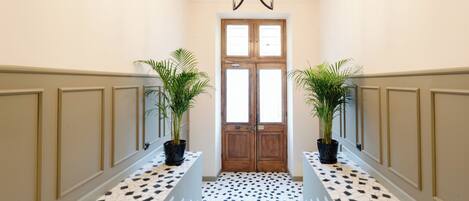 Um corredor com piso estampado, uma porta de madeira e duas plantas em vasos.