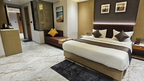 Quarto de hotel moderno com uma cama grande, uma mesa de cabeceira, escrivaninha, sofá e uma janela ampla.