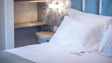 Cama bem arrumada com lençóis brancos e um travesseiro com logo, uma mesa de cabeceira e uma parede com papel de parede estampado.
