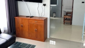 Uma sala de estar moderna com uma televisão de tela plana na parede, um armário de madeira, uma mesa de centro de vidro e um sofá preto.