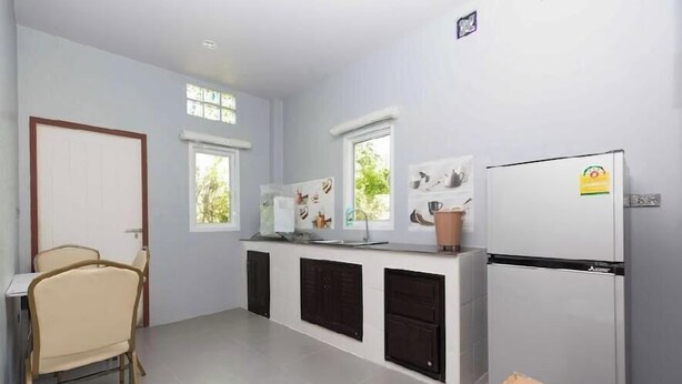 Cozinha com geladeira branca, mesa de jantar com cadeiras e janela com vista para o verde.