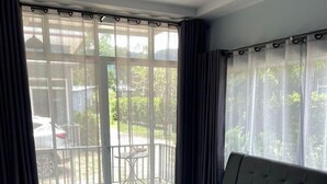 Uma sala de estar moderna com uma mesa de centro de vidro, um sofá escuro e grandes janelas com cortinas.