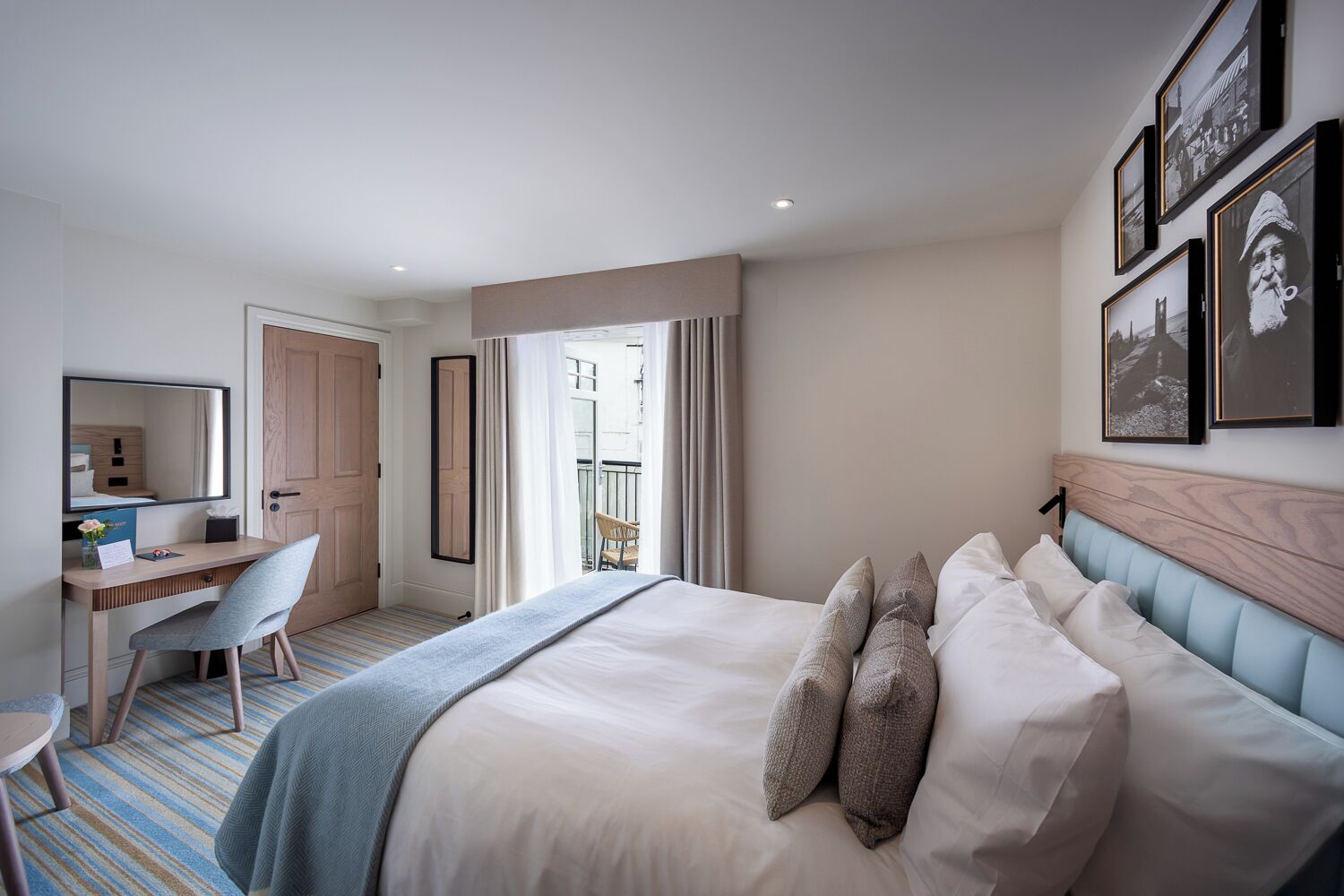 Quarto de hotel com cama, escrivaninha, cadeira, espelho e porta.