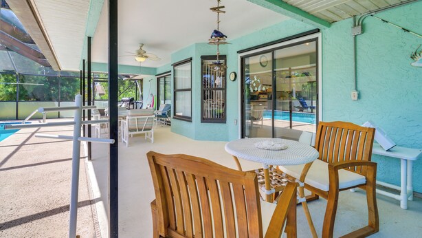 Uma área externa coberta com piscina, cadeiras de madeira e uma mesa.