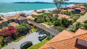 Uma área residencial costeira com casas de telhado em terracota, vista clara do oceano e uma rua pavimentada com veículos estacionados.
