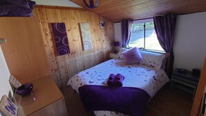 Quarto com painéis de madeira, cama, toalhas roxas e janela com cortinas.