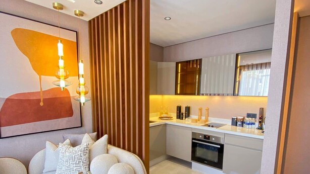 Uma sala de estar moderna com um sofá, uma mesa de centro e uma cadeira vermelha. Na parte de trás, há uma cozinha com pia e fogão.