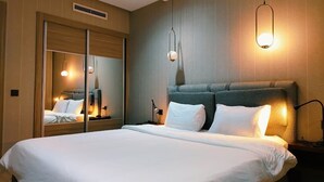 Quarto de hotel com uma cama grande, um espelho e duas luminárias fixadas na parede.