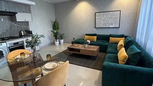 Uma sala de estar moderna com um sofá verde, uma mesa de jantar de vidro e uma área de cozinha com fogão.