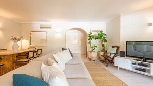 Uma sala de estar moderna com sofá, televisão, área de refeições e uma planta.