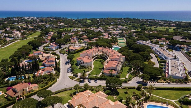 Vista aérea de uma área residencial costeira, com casas, ruas e uma grande extensão de água ao fundo.