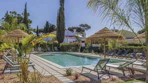Uma área de piscina com espreguiçadeiras, piscina e guarda-sóis de palha.