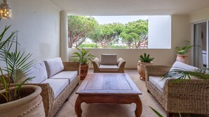 Varanda com móveis de vime, mesa de centro de madeira e plantas em vasos.