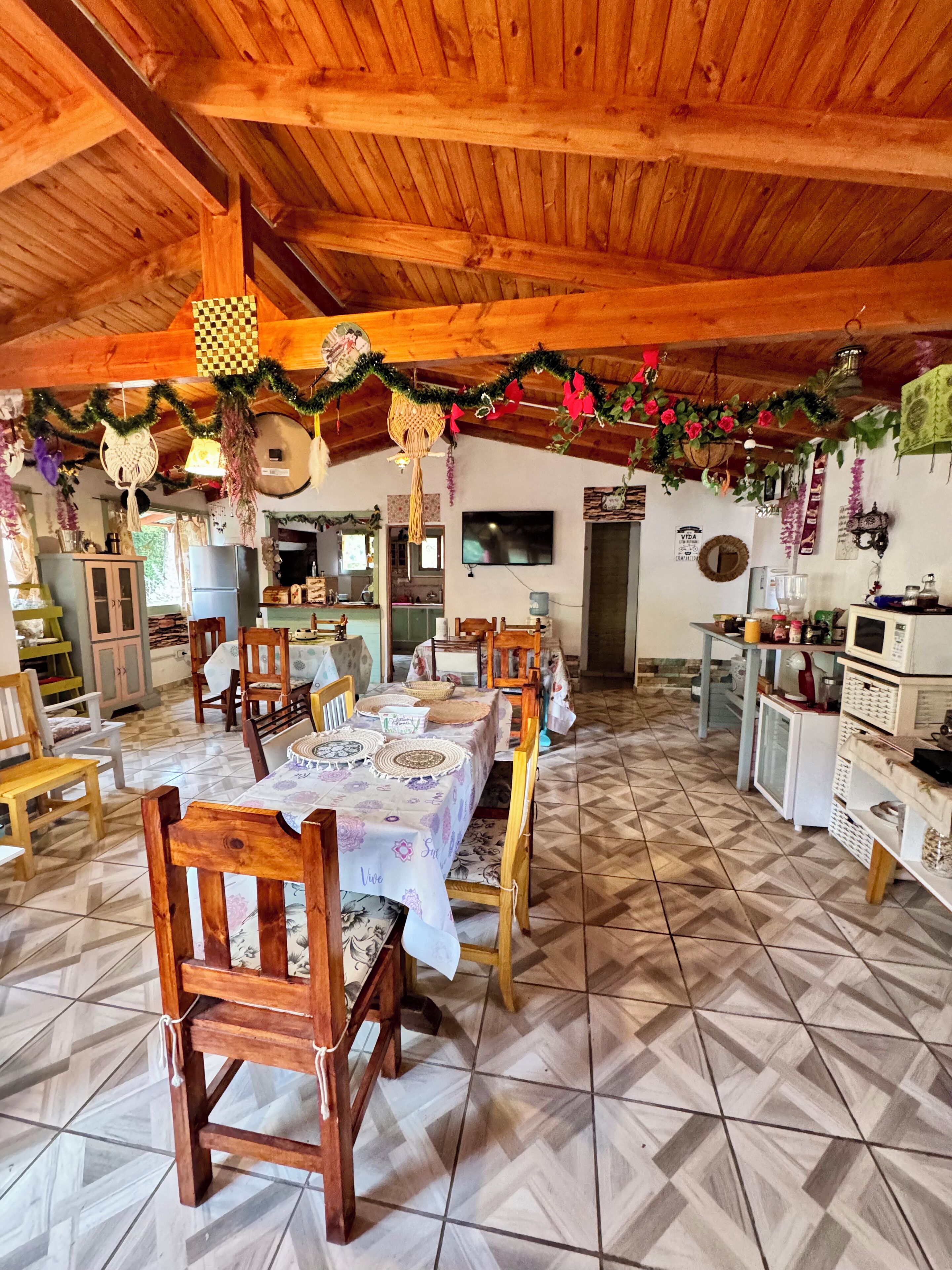 Uma área de jantar rústica com mesas e cadeiras de madeira, piso ladrilhado e teto de madeira.