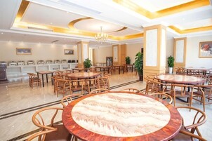 Espaço de refeições de hotel com mesas e cadeiras redondas, um candelabro e um balcão de buffet.