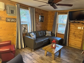 Um quarto acolhedor em estilo cabana, com um sofá de couro, uma mesa de centro de madeira e um ventilador de teto.