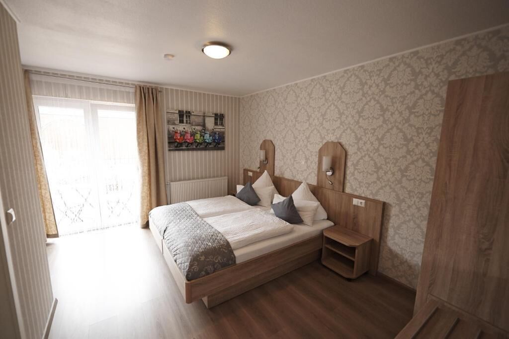 Quarto com cama de madeira, mesas de cabeceira, radiador e janela com cortinas.