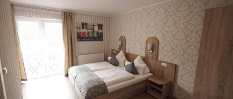 Quarto com cama de madeira, mesas de cabeceira, radiador e janela com cortinas.