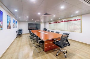Sala de conferência com uma mesa comprida, cadeiras, tela de projetor e um mural com a programação.