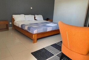 Quarto com cama de madeira, mesa de cabeceira, cadeira e tapete estampado.