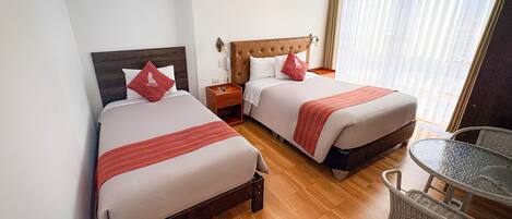 Quarto de hotel com duas camas, uma mesinha e vista para o exterior.
