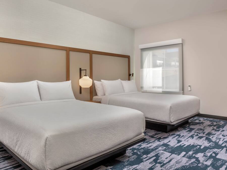 Quarto de hotel com duas camas, uma janela ampla e um luminário moderno.